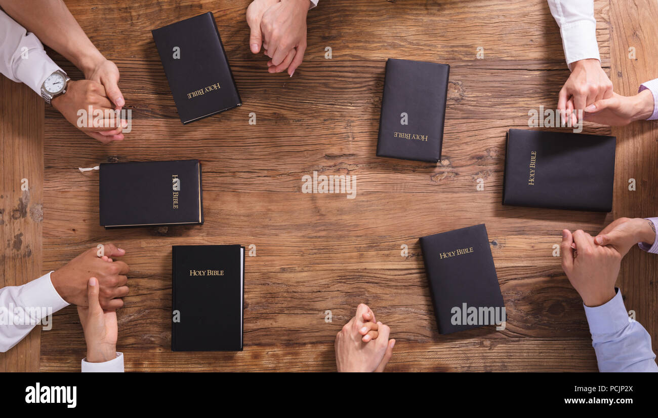High Angle View Of People's Praying Hands On Holy Bible Stock Photo - Alamy