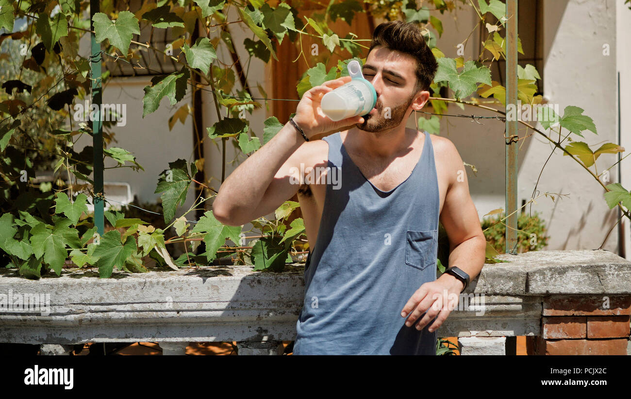 Young man drinking protein shake from blender outside in summer day ...