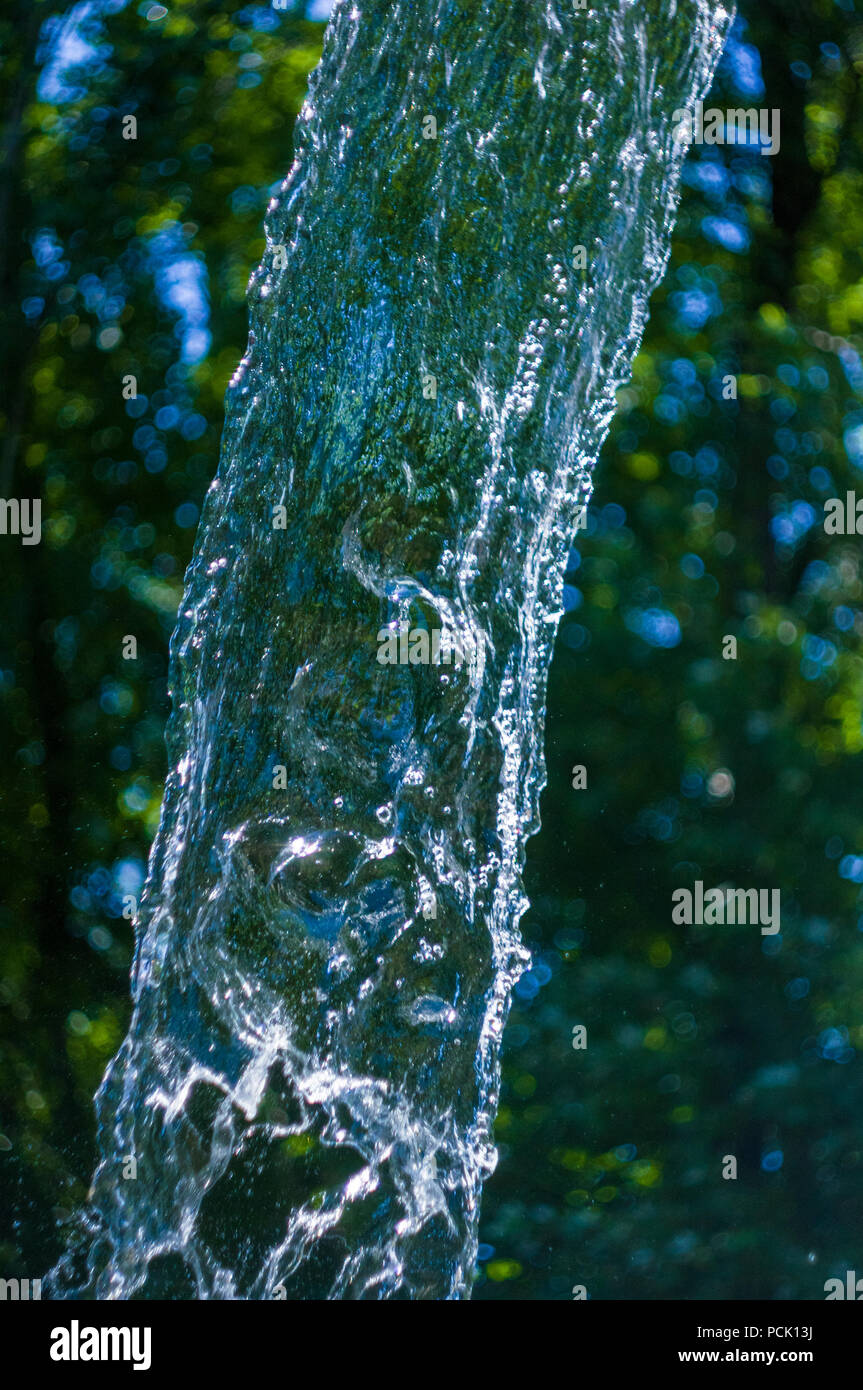 transparent falling water vertical flows against a blue sky and green ...