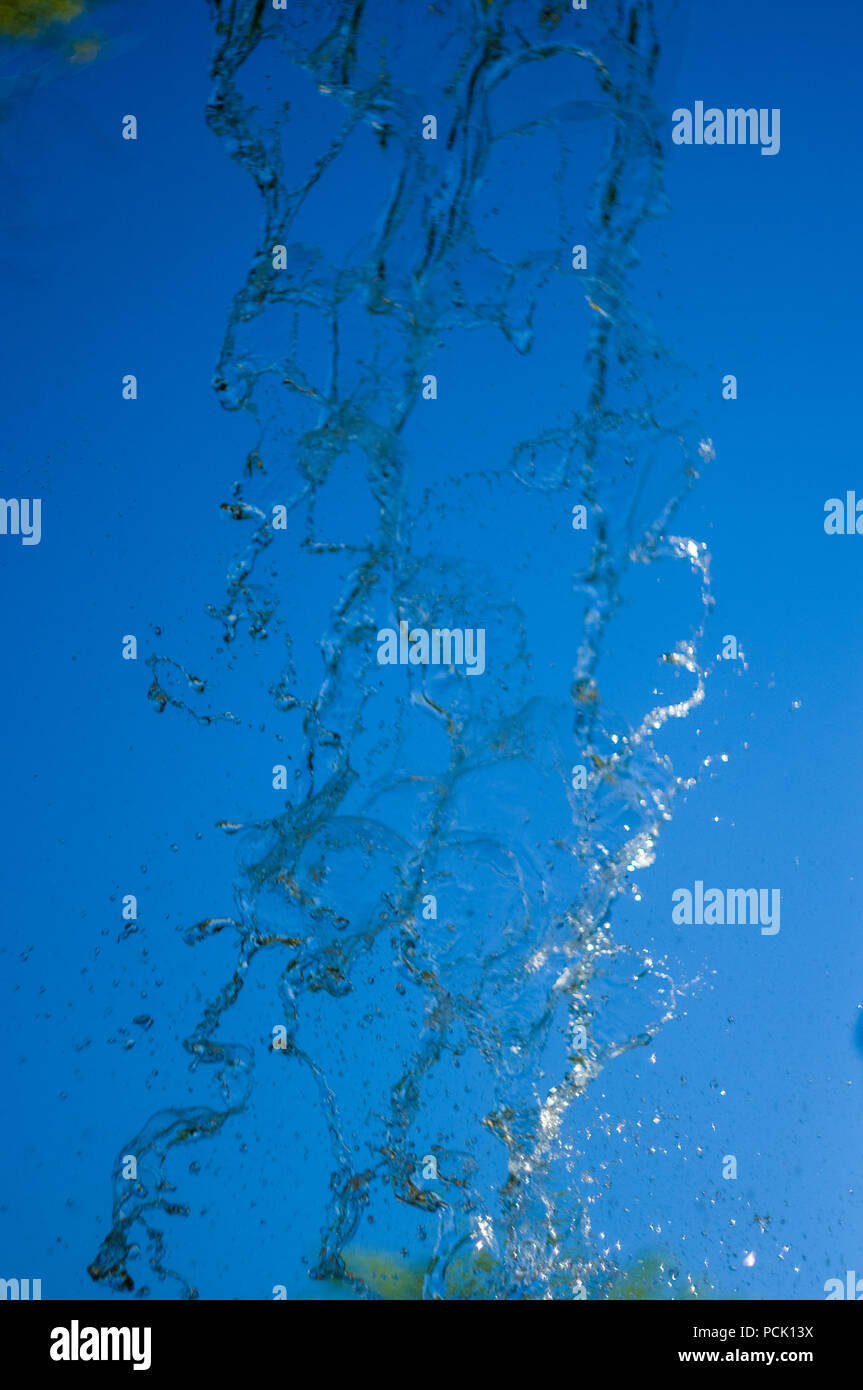 transparent falling water vertical flows against a blue sky and green ...
