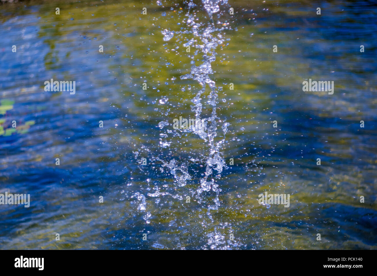 transparent falling water vertical flows against a blue sky and green ...