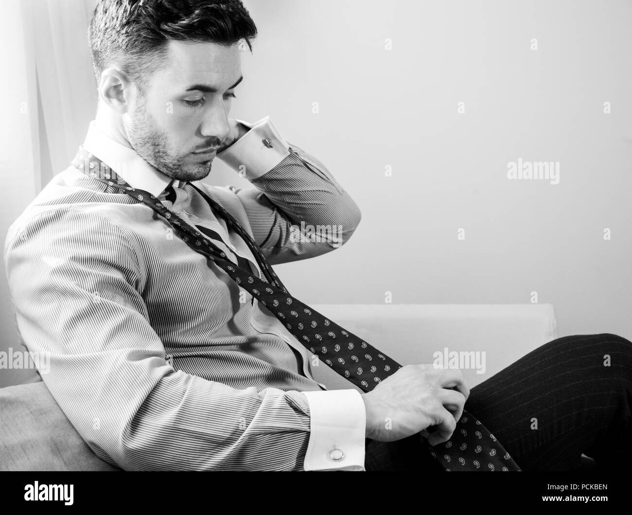 Handsome businessman wearing tie and open shirt sits in front of window ...