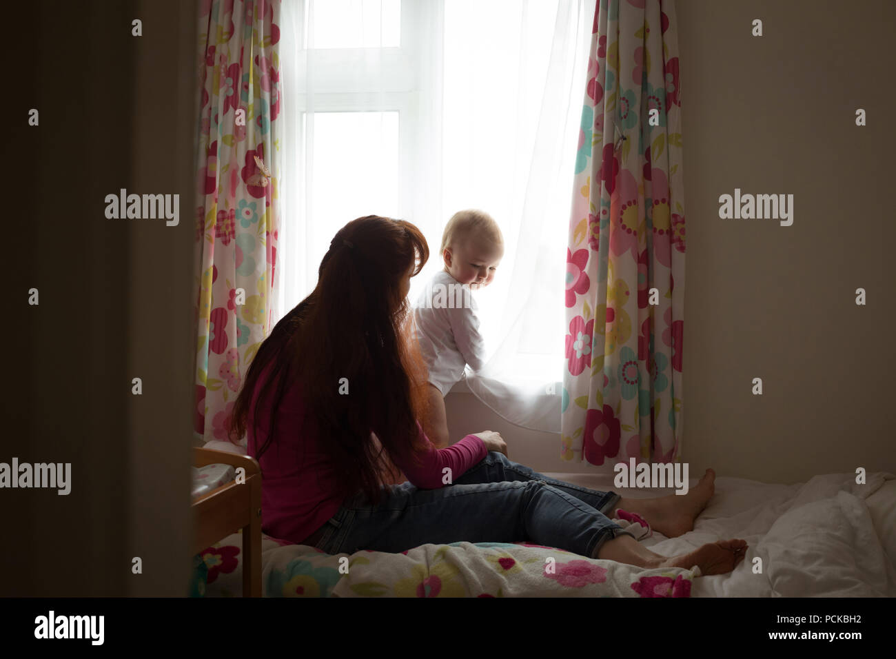 Mother with her baby girl looking through window Stock Photo - Alamy