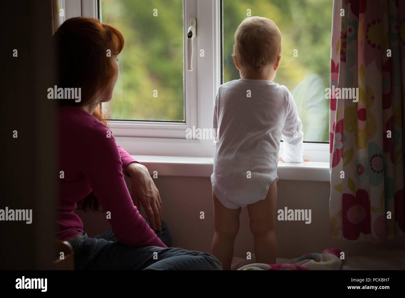 Mother with her baby girl looking through window Stock Photo - Alamy