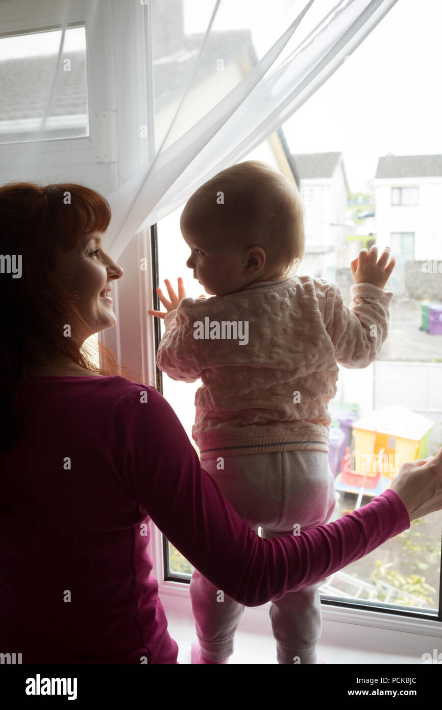Mother with her baby girl looking through window Stock Photo - Alamy
