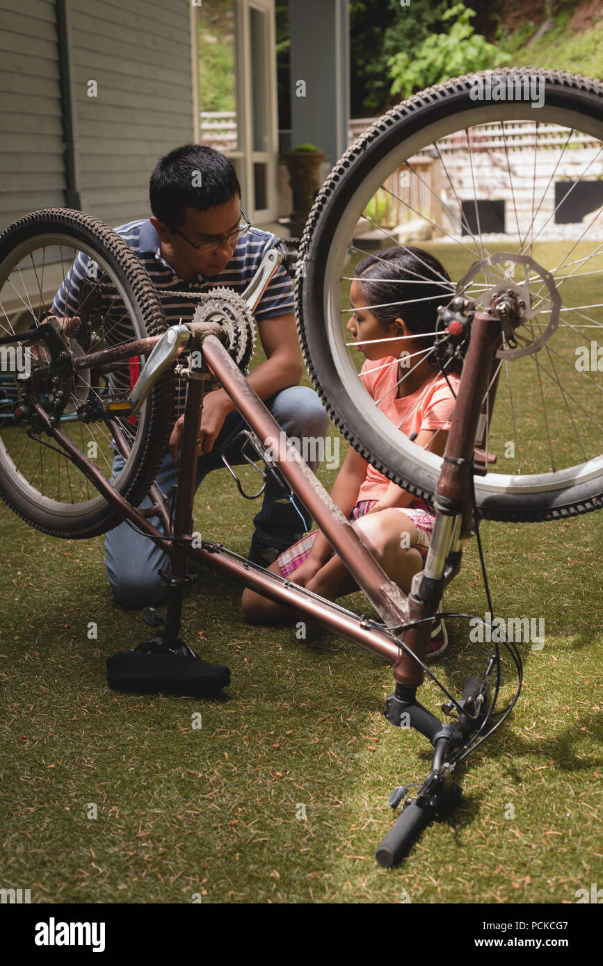 Father and daughter interacting with each other while repairing cycle ...