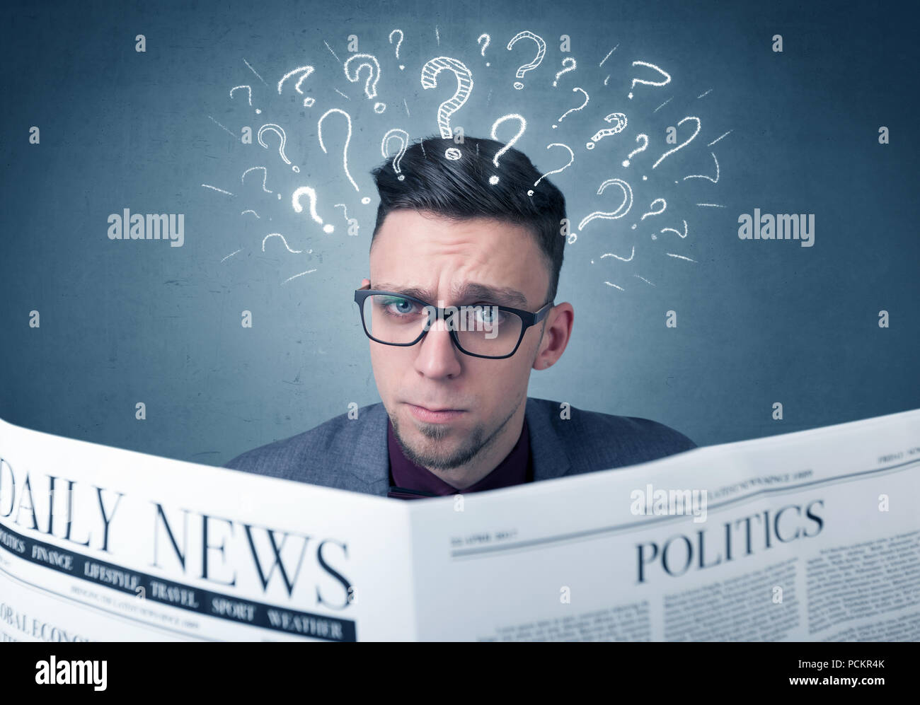 Young confused businessman reading daily newspaper with question marks ...