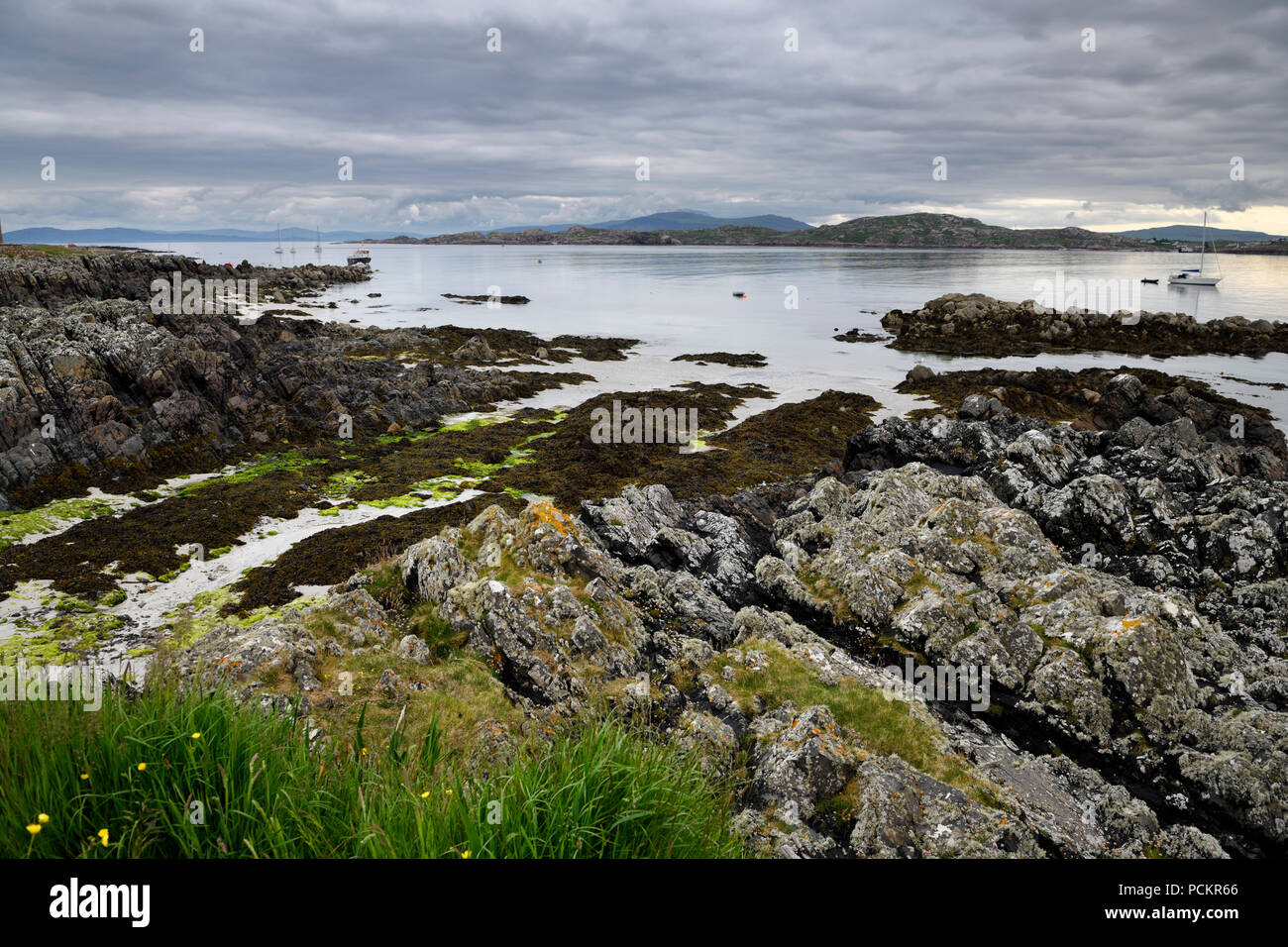 Sand beach and rocky shore under clouds on Isle of Iona with boats on ...