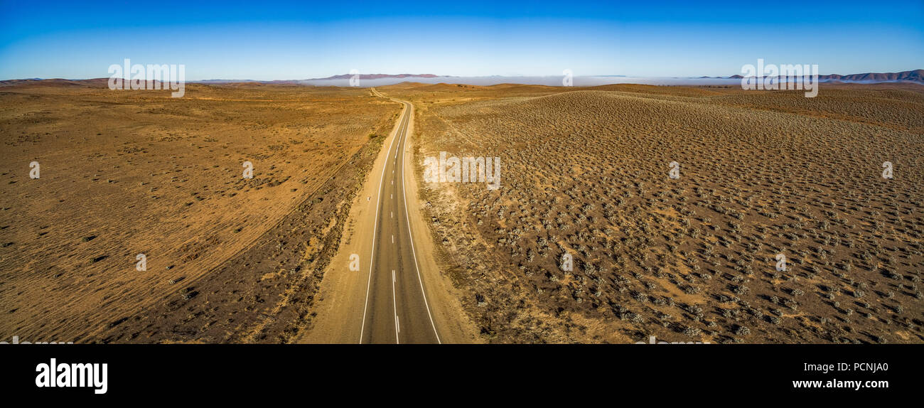 Rural road passing through dry land with scarce vegetation at sunrise ...