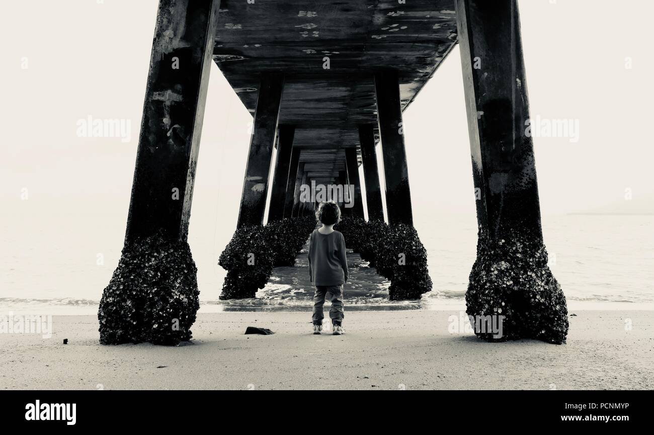 A young child standing under a jetty near the ocean, The Cardwell Jetty ...
