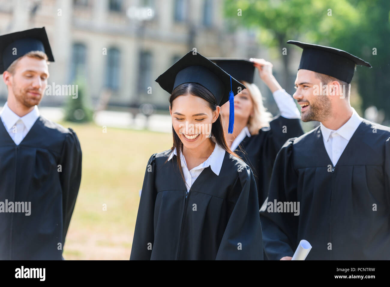smiling young graduated students in capes on university garden Stock ...