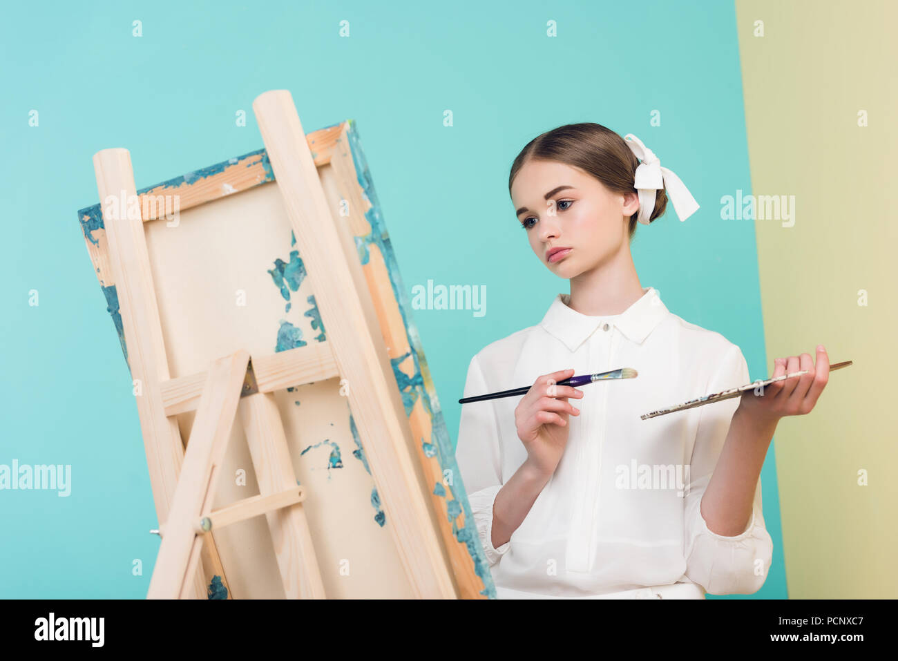beautiful teen artist painting on easel with brush and palette, on ...