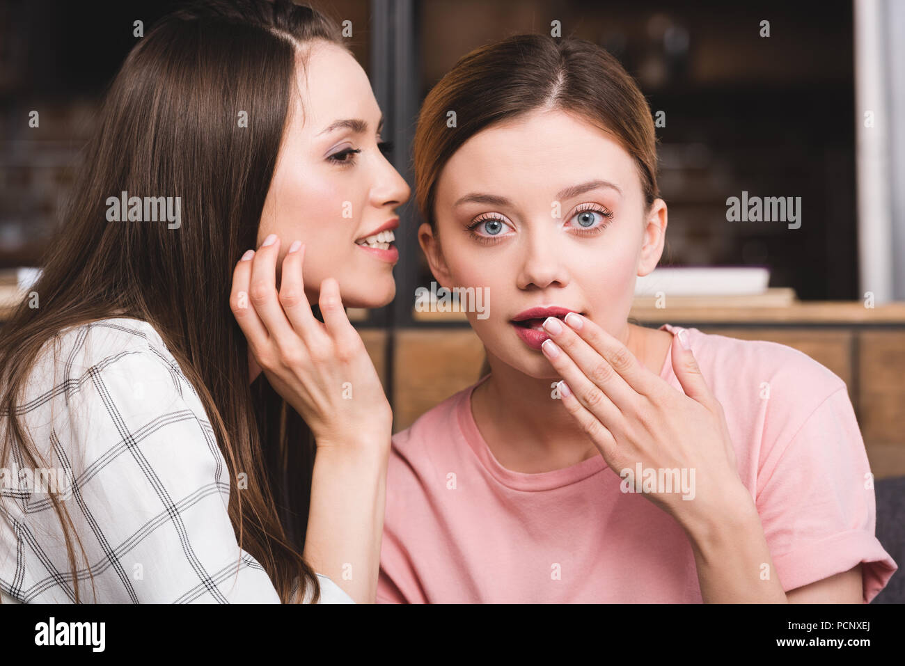 side view of young woman whispering secret to surprised female friend ...