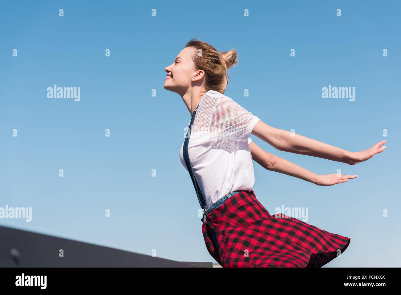 side view of happy young woman with wide arms standing against blue sky ...