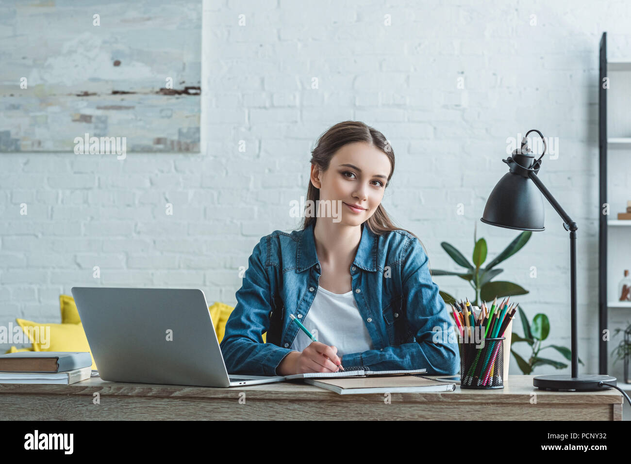 teenage girl taking notes and smiling at camera while studying with ...