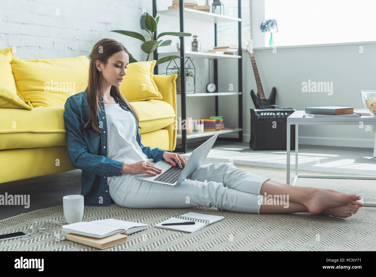 concentrated barefoot girl using laptop while sitting on carpet and ...
