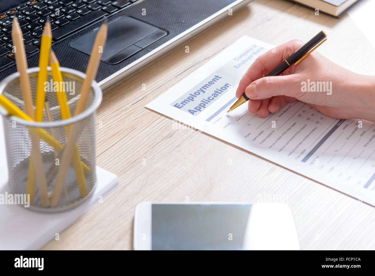 Filling in blank employment application form on a desk Stock Photo - Alamy