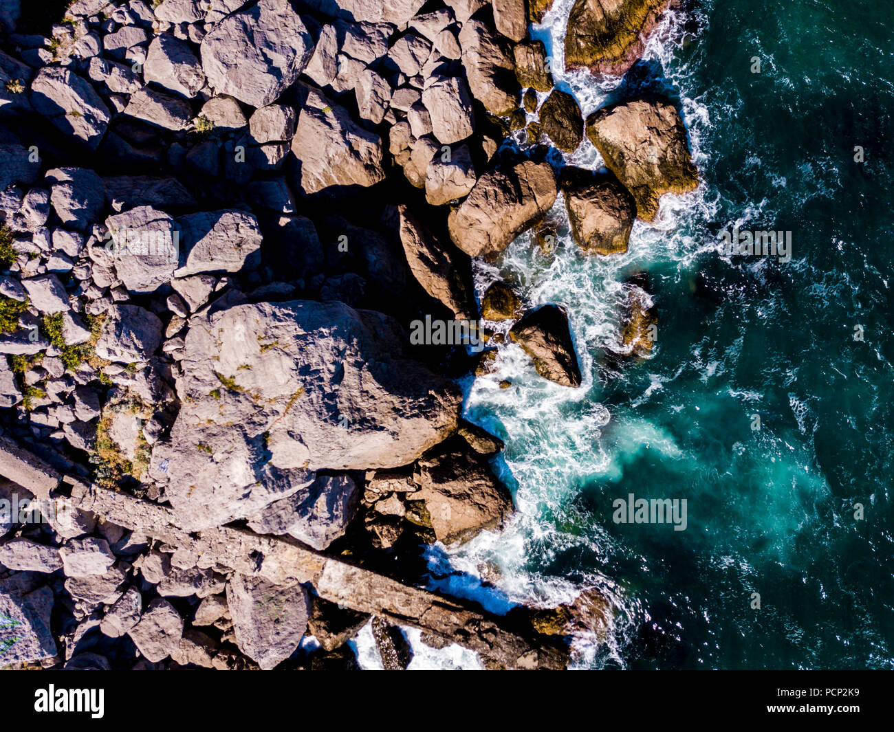 aerial overhead view of waves crash into the stone rocky sea coast ...