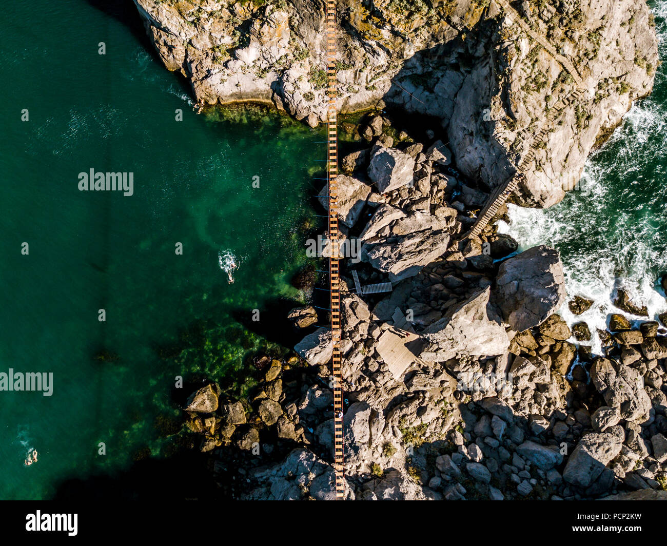 unrecognizable man walking on the rope bridge over the sea water aerial ...