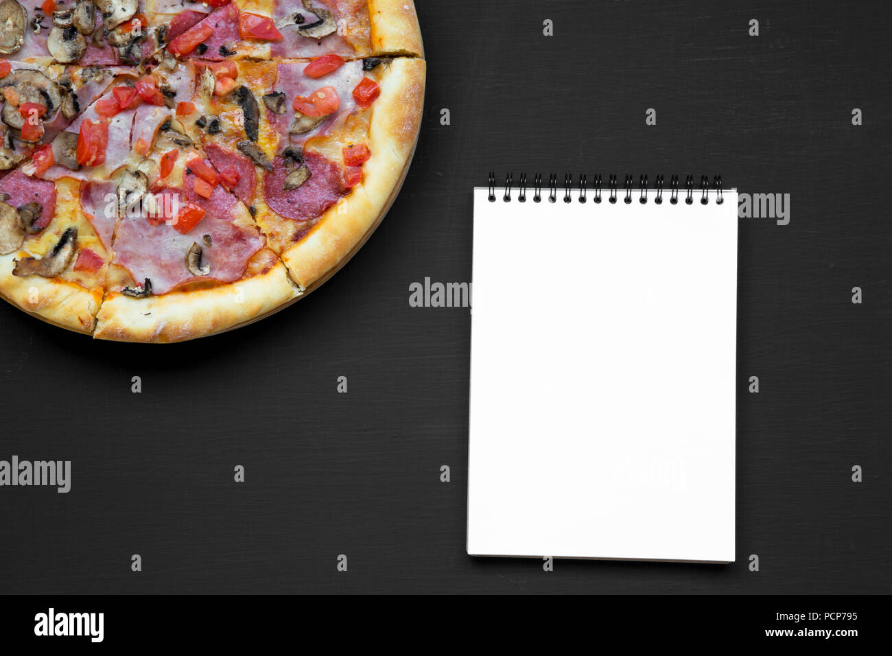 Overhead view, freshly baked pizza with notepad on black table. Flat ...