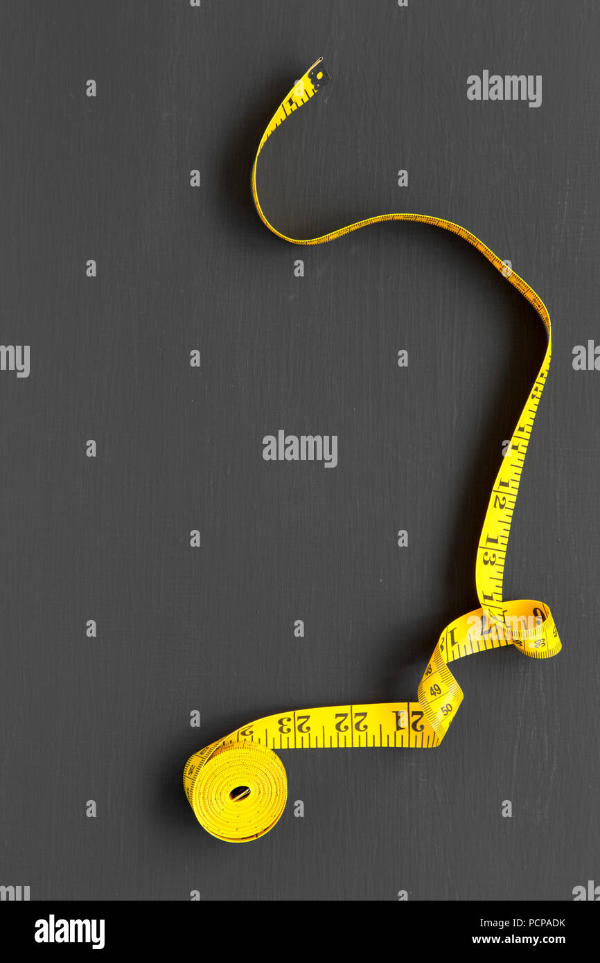 Top view, yellow measuring tape on black background. From above. Copy ...