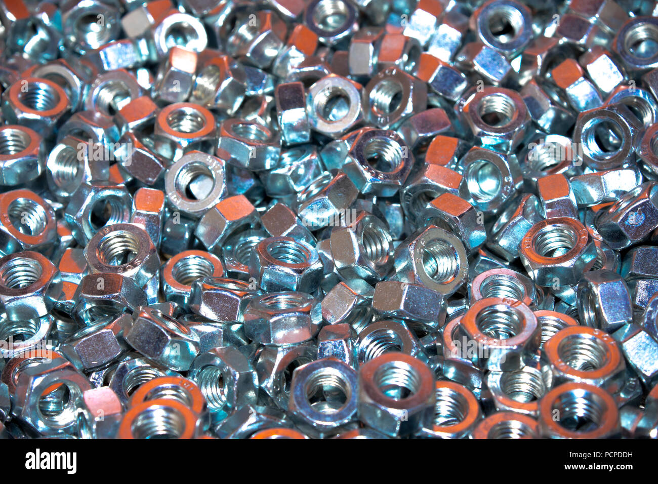Lots of industrial galvanized steel nuts on a a big pile in warm light ...