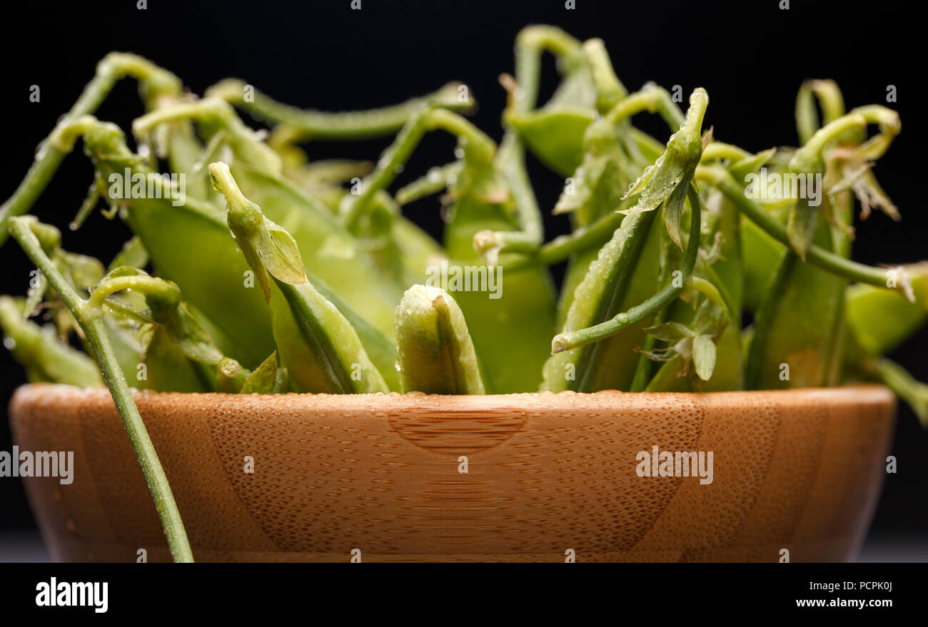 Photo of green pea pods in wooden cup on blank black background in ...