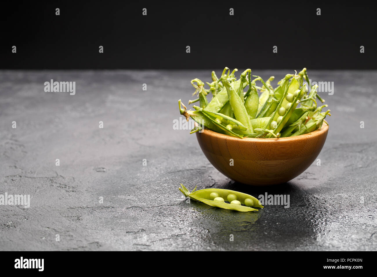 Photo of green pea pods in wooden plate on blank black table with pod ...