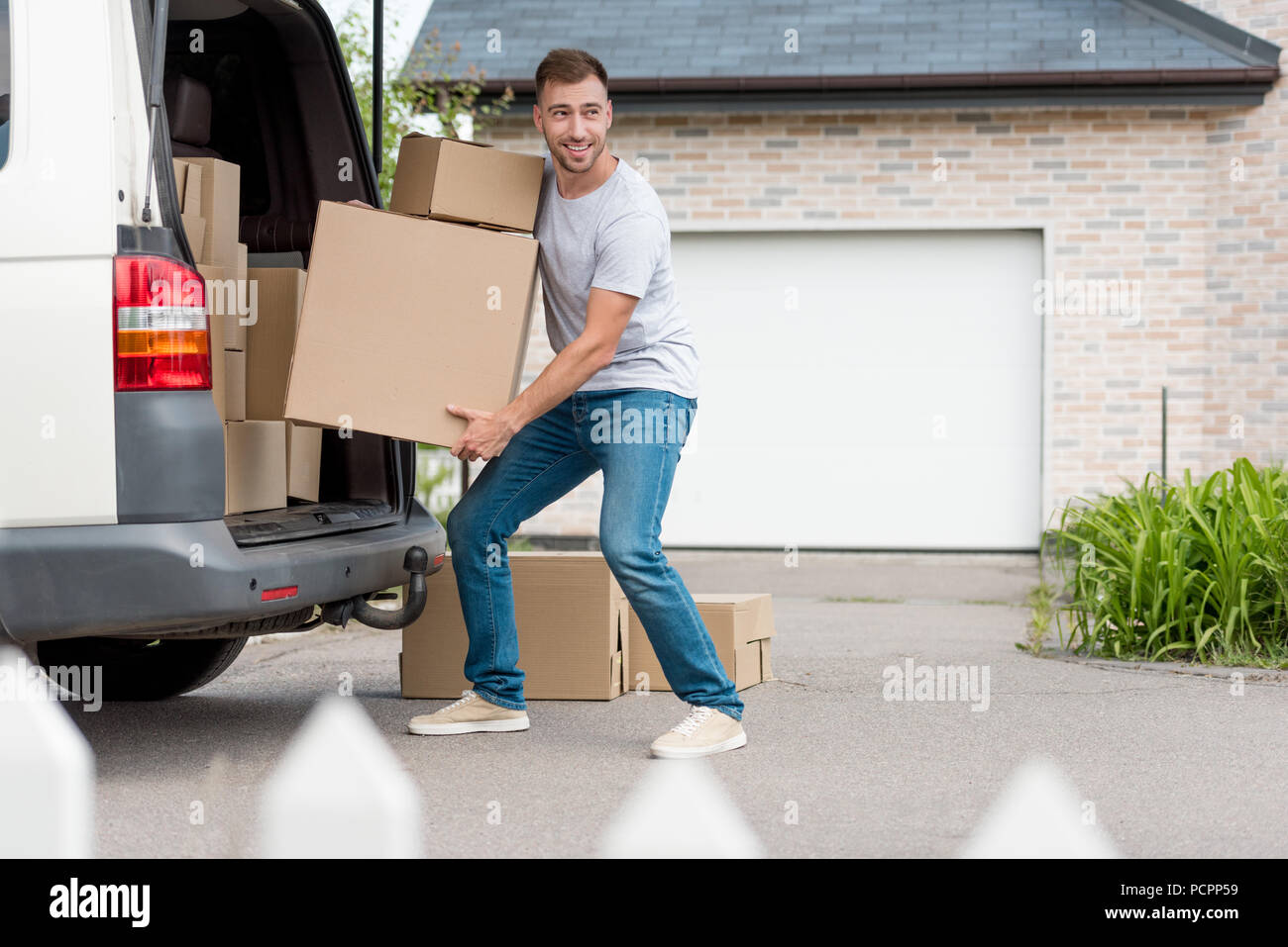 young smiling man moving boxes from car into new house Stock Photo - Alamy