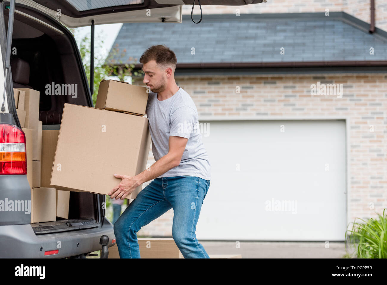 strenuous young man moving boxes from car into new house Stock Photo ...