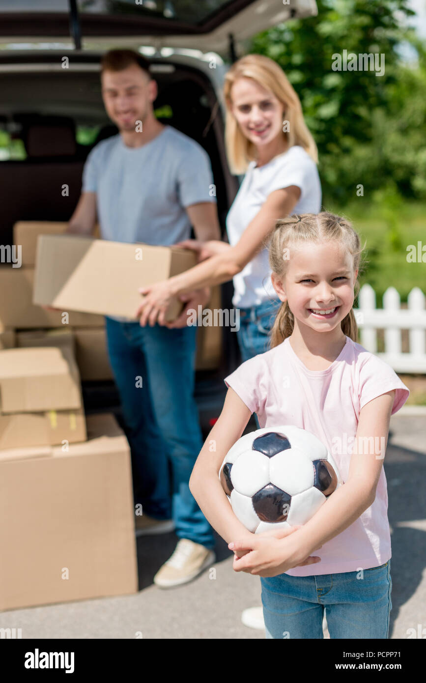 happy little kid holding soccer ball while her parents unpacking ...