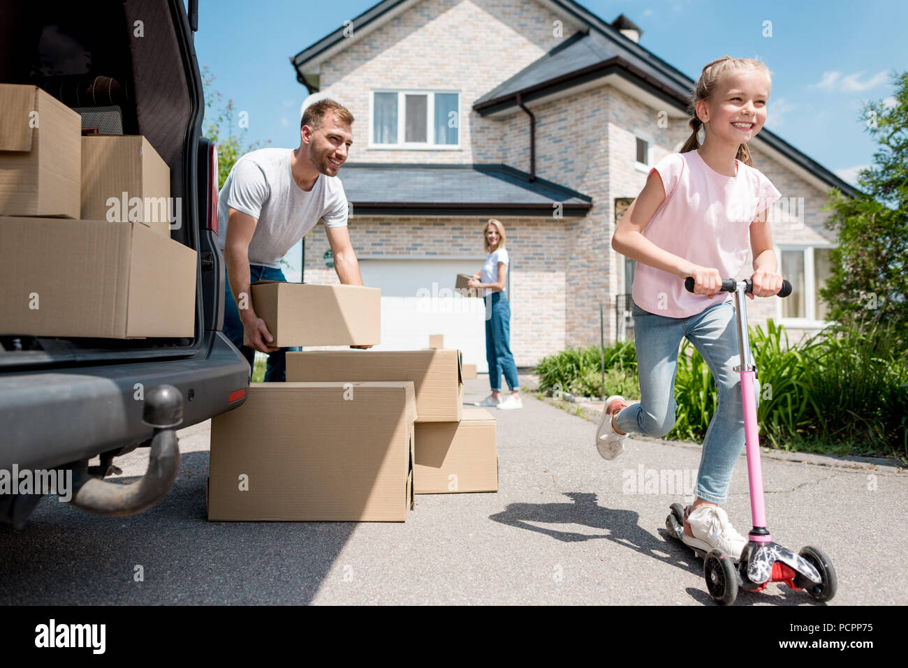 close up view of little kid riding on kick scooter and her parents ...