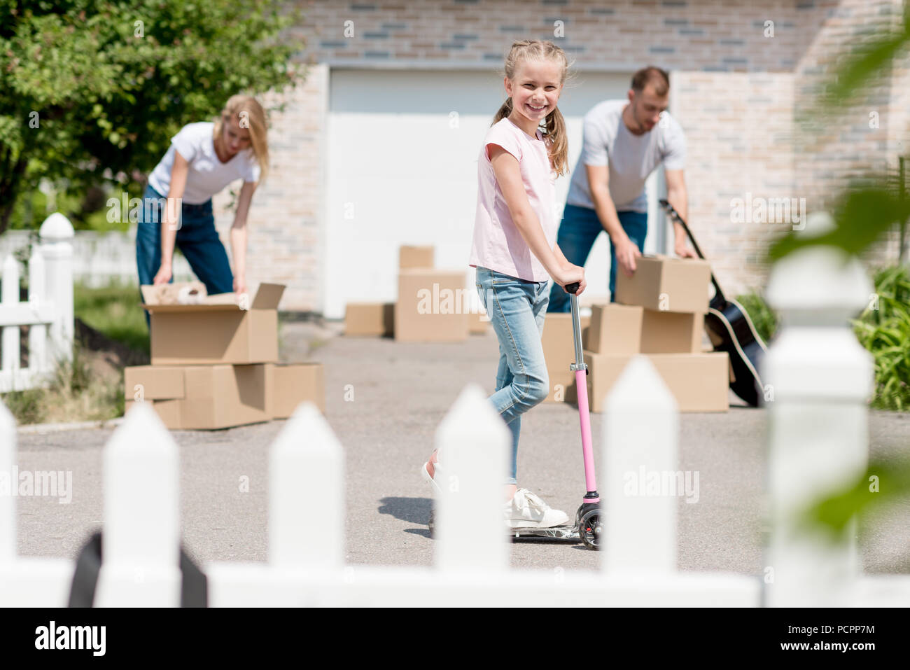 couple unpacking cardboard boxes while their smiling daughter riding on ...