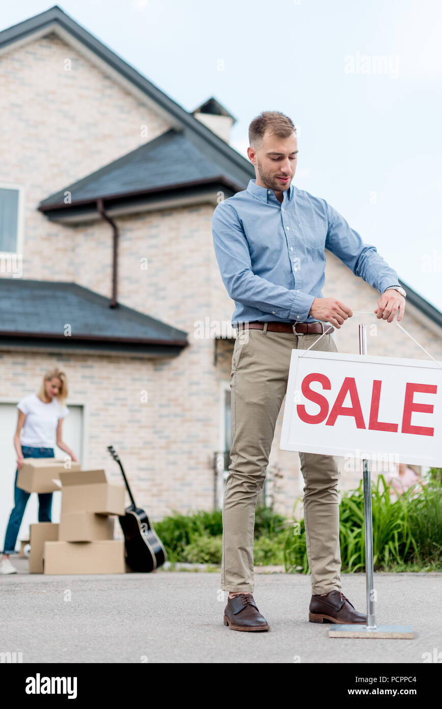 male realtor hanging sale sign in front of woman packing cardboard ...