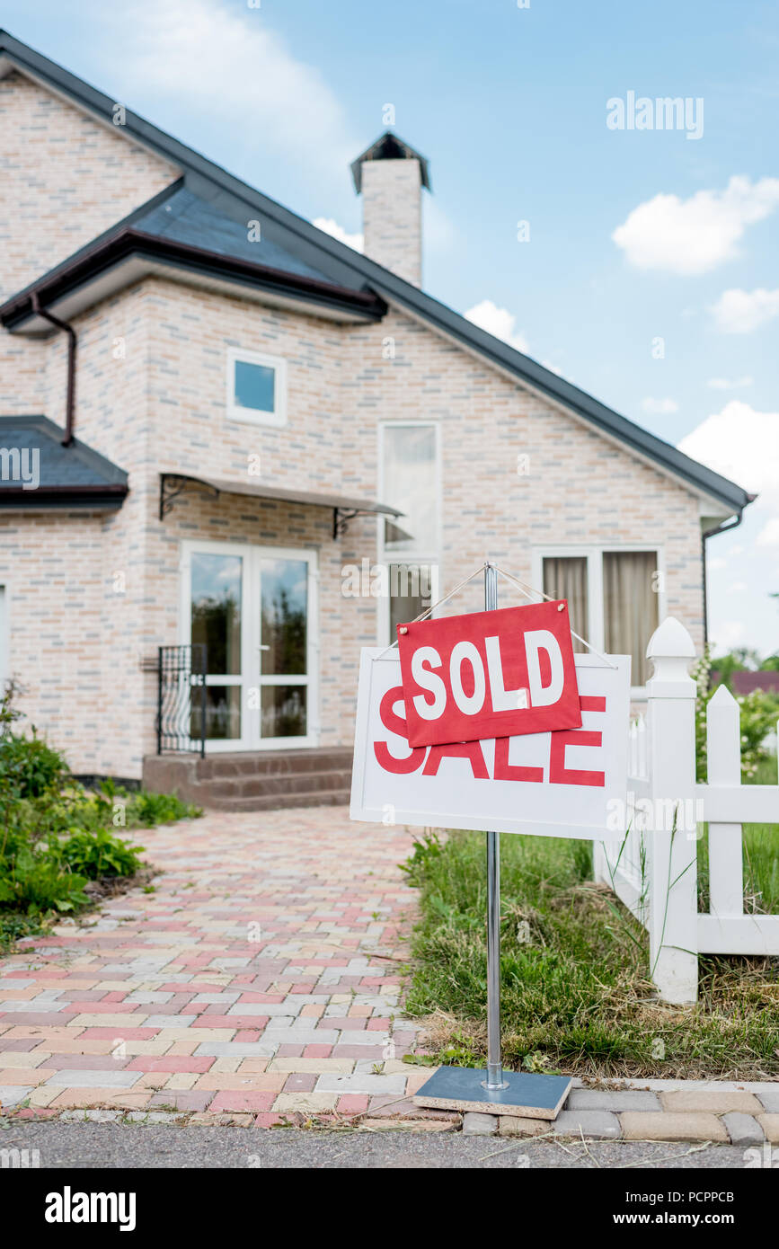 sold sign on wooden placard with sale sign in front of modern cottage ...
