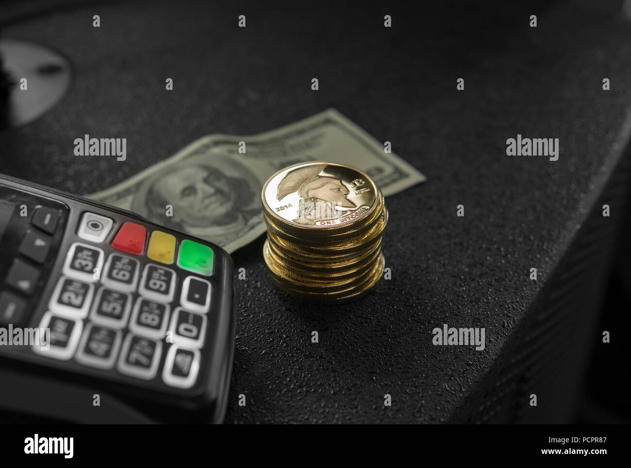 A pile of gold Titan coins and POS terminal with a hindred dollar ...