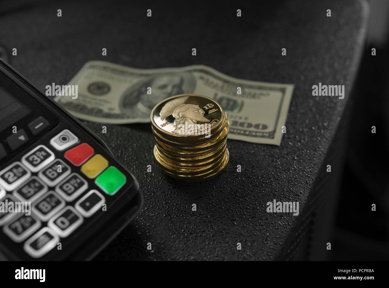 A pile of gold Titan coins and POS terminal with a hindred dollar ...