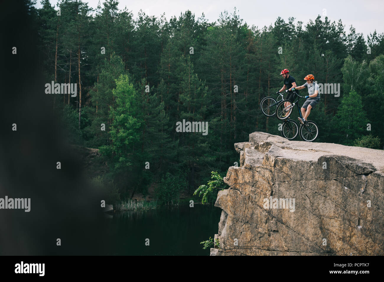 side view of extreme trial bikers standing on back wheels on rocky ...