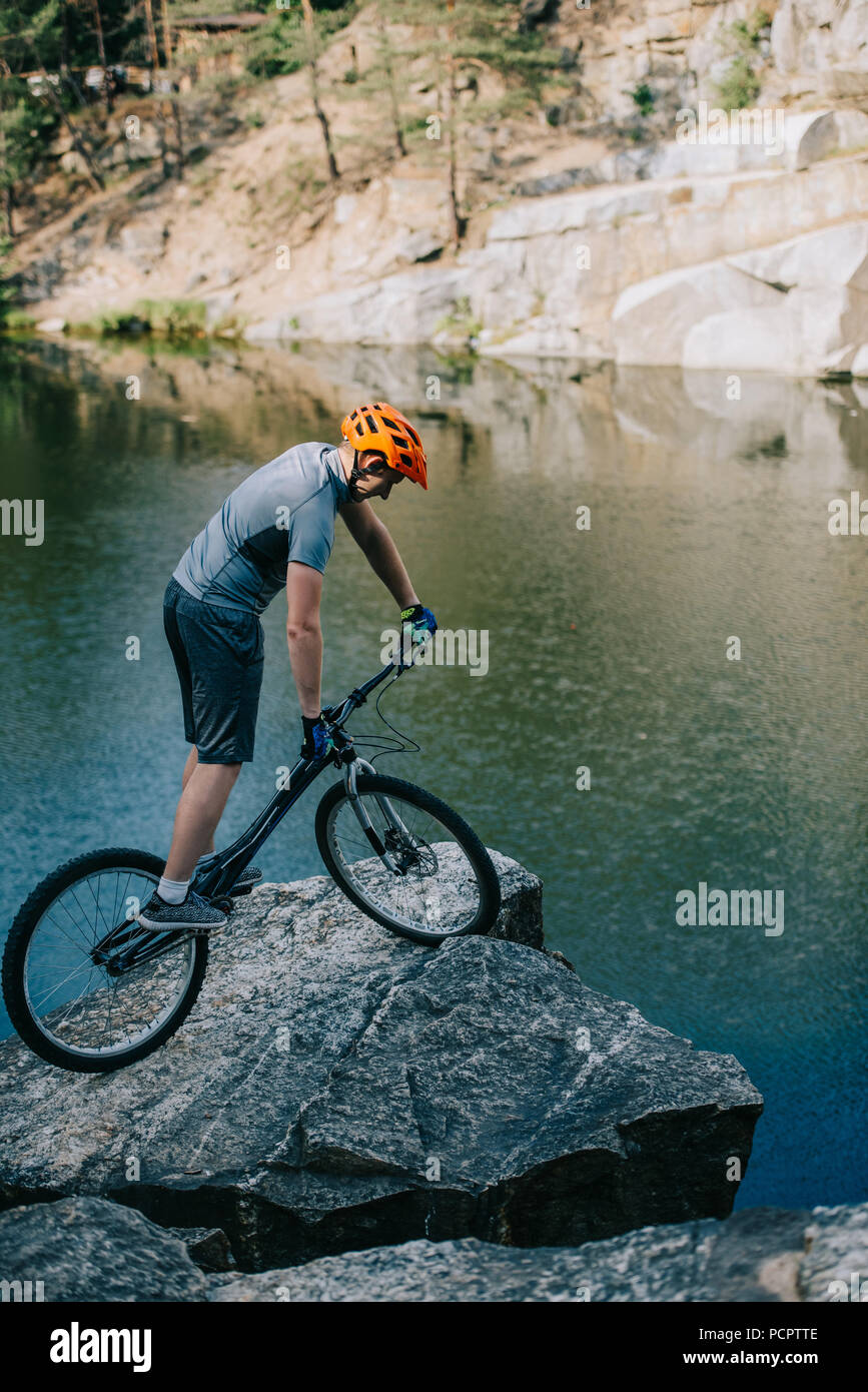 athletic trial biker balancing on rocky cliff over lake Stock Photo - Alamy