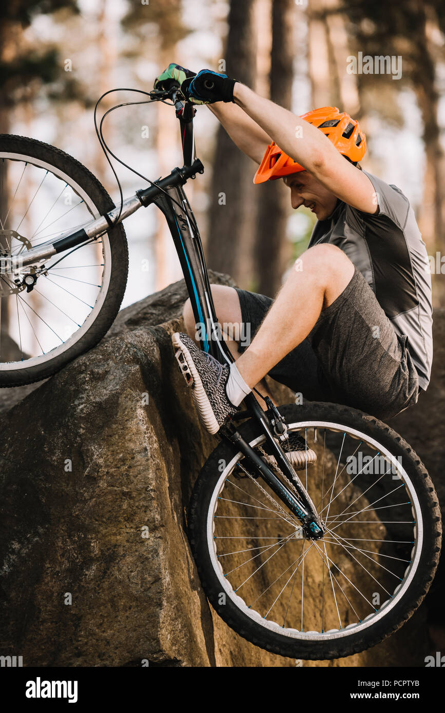 young trial biker climbing on rock with bicycle outdoors Stock Photo ...