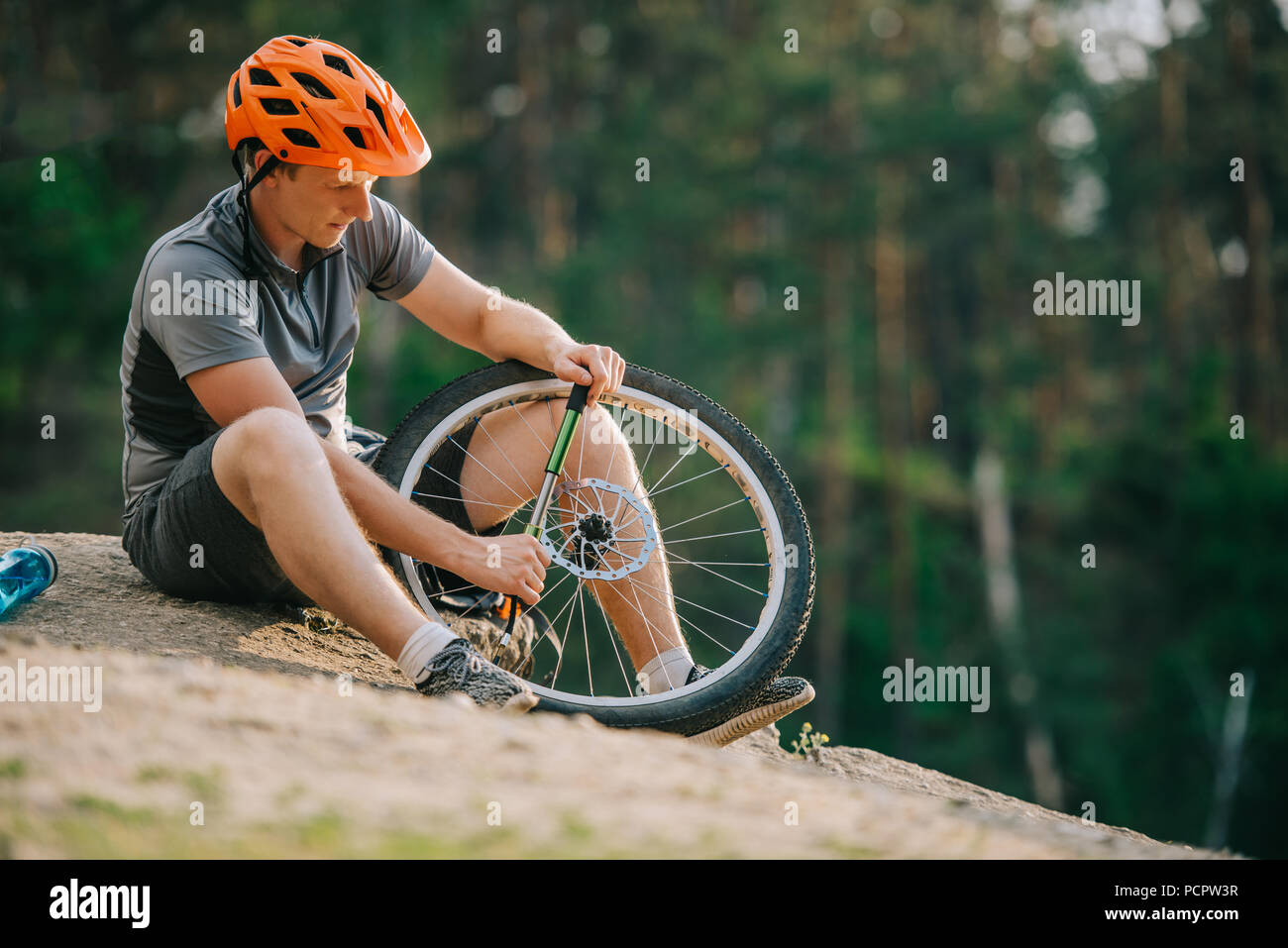 young trial biker pumping wheel of bicycle outdoors while sitting on ...