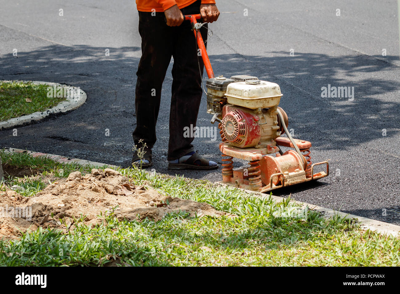 Worker uses vibratory plate compactor compacting asphalt at road repair ...