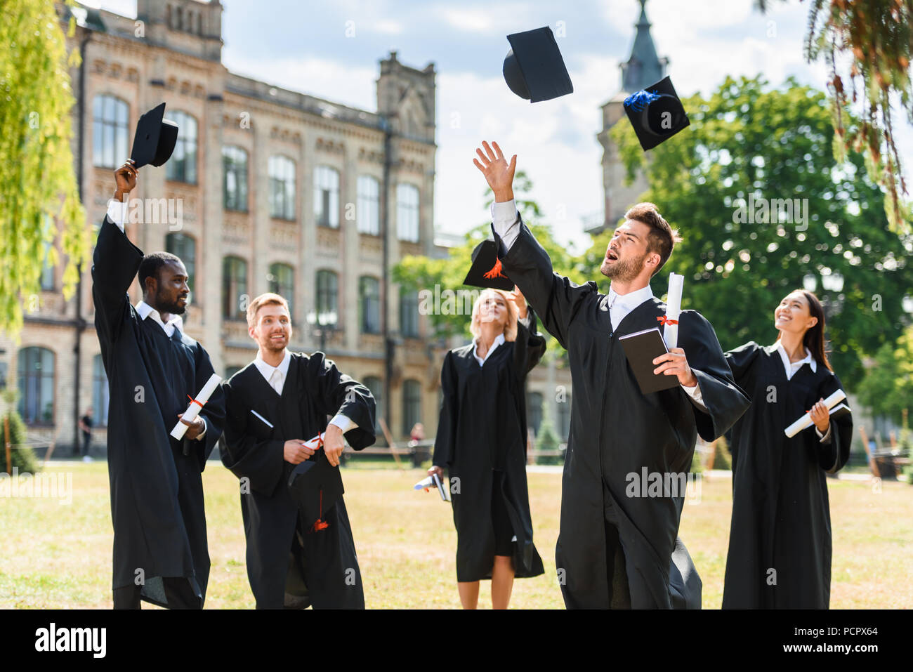 young happy graduated students throwing up graduation caps in ...