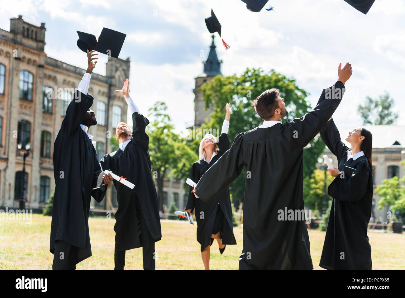 young graduated students throwing up graduation caps in university ...