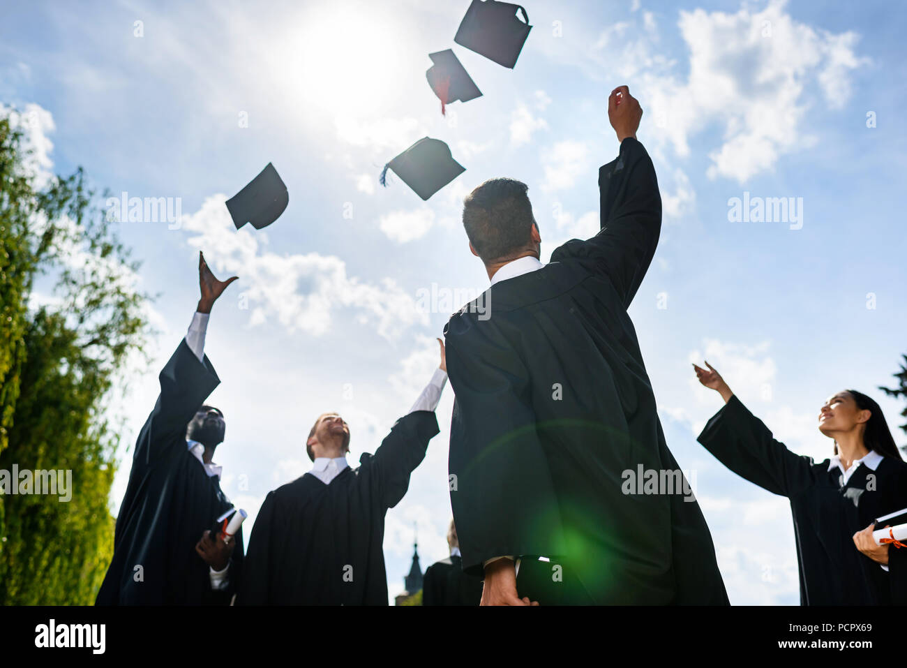 bottom view of young graduated students throwing up hats in front of ...