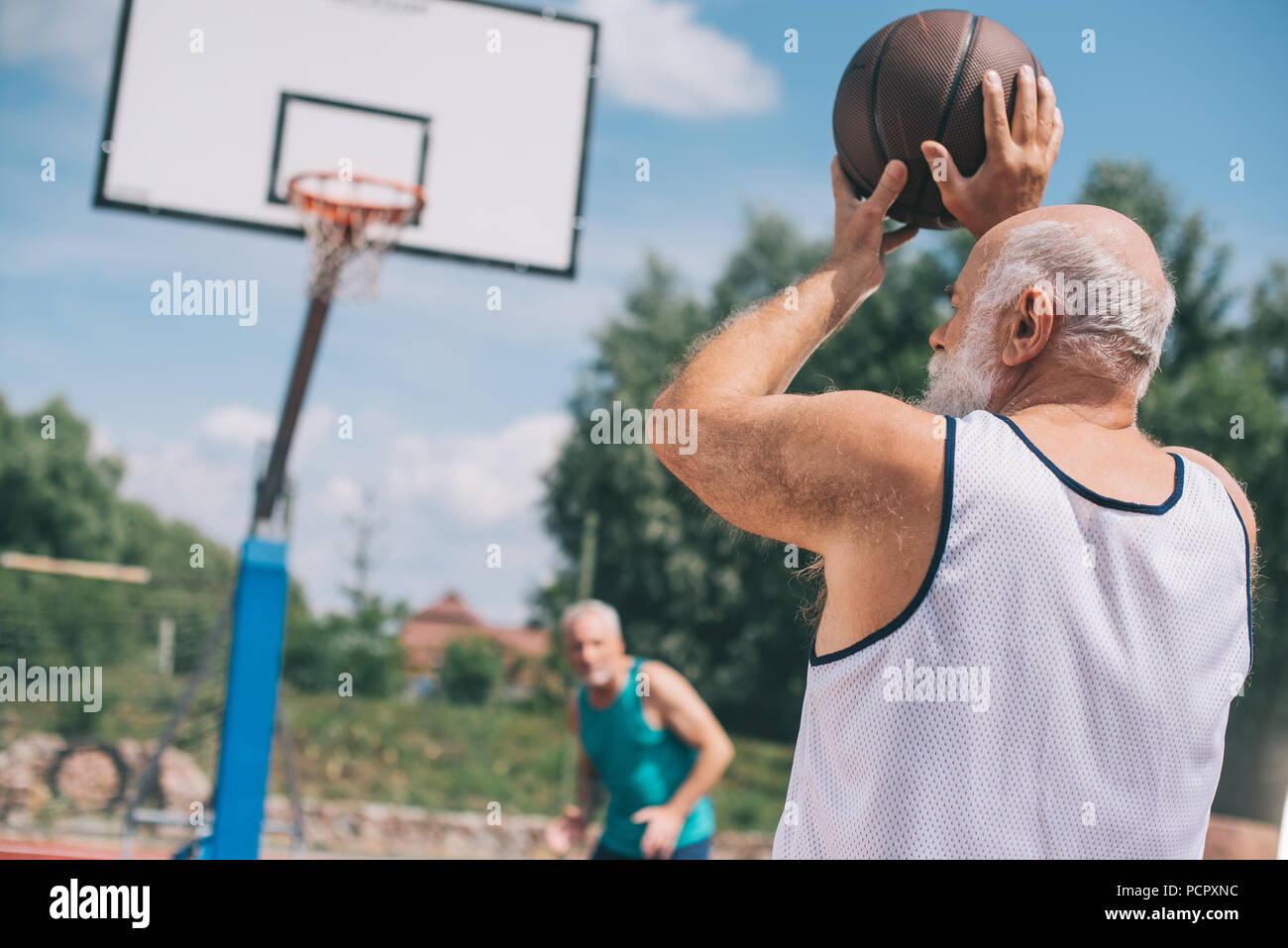 elderly men playing basketball together on playground on summer day ...