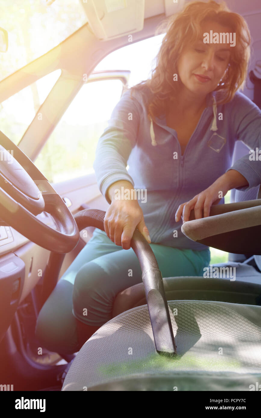 Woman hoovering a seat inside a car cabin, visible dirt. Cleaning car ...
