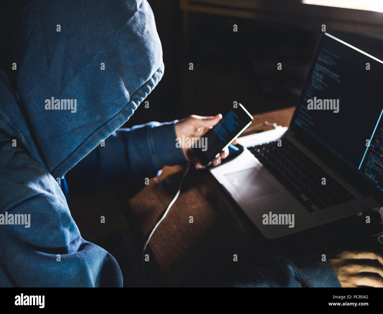 anonymous person in the hood sitting in front of computer working with ...