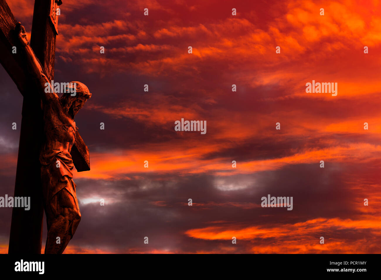 Jesus on a cross against burning red sunset sky with clouds and little ...