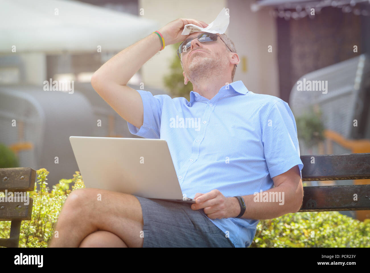Man suffers from heat while working with laptop outside and wiping his ...